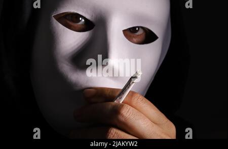 masked man smoking cigarette on dark background Stock Photo - Alamy