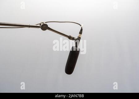 An isolated studio microphone hanging from above by it's cord facing ...