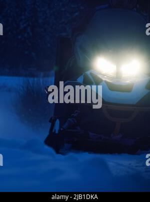 Two snowmobiles rides on a snowy forest road at night with its ...