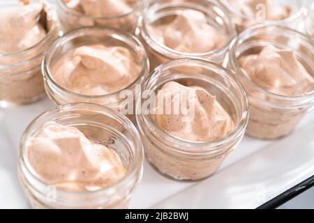 Scooping mixture into the small glass jars to make homemade chocolate ...