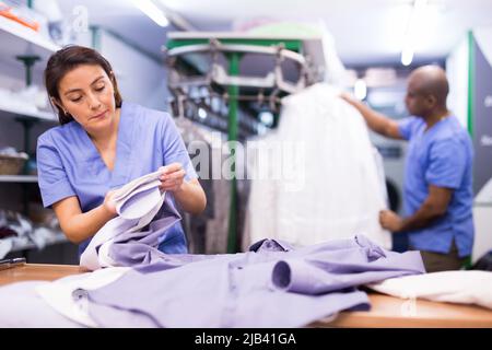 Focused woman dry-cleaning worker checking clean clothes Stock Photo ...