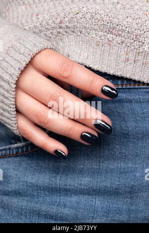 Female hand with long nails and dark blue teal manicure holds a bottle ...