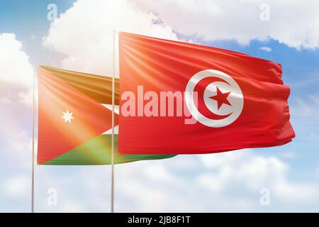 Tunisia and Jordan flags waving together in the wind on blue cloudy sky ...