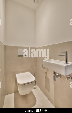 White ceramic toilet placed at white tiled wall in light stylish ...