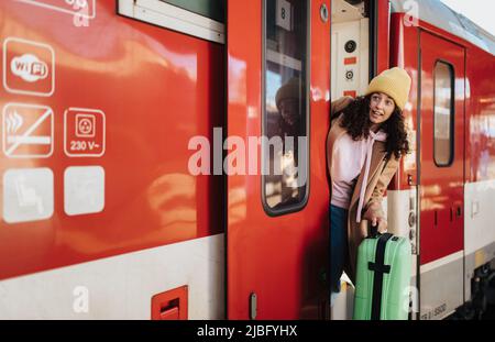 Woman with suitcase getting off passenger train at train station Stock ...