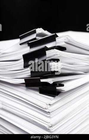 A stack of office papers, some of which are fastened with black binders ...