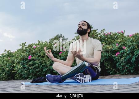 Young man with a prosthetic leg doing stretching exercises outdoors ...