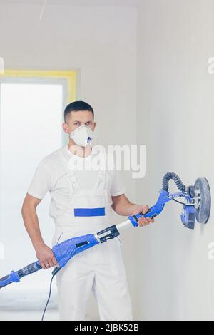 Man smoothes wall surface with a wall grinder. Male grind a white ...