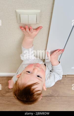 Toddler baby boy reaches for the light switch. Child turns on the light ...