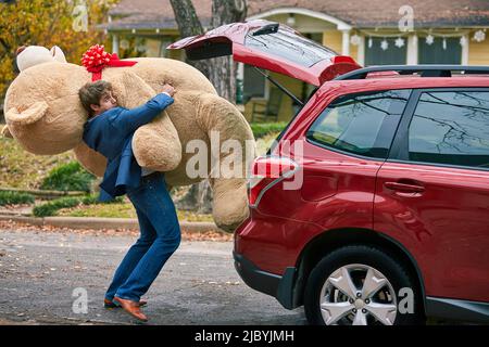 A goofy young man struggling to pull out an oversized teddy bear ...