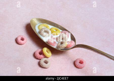 Fruit-flavoured cereal rings in spoon and glass of milk, children's ...