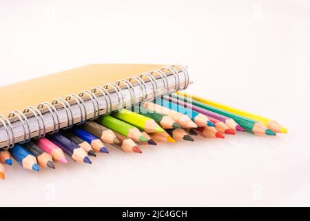 Color pencils of various colors near a notebook on a white background ...