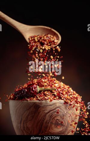 Chilli flakes are poured into a wooden dish. Chilli flakes and dried ...