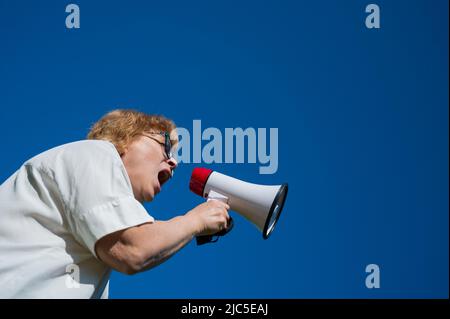 Emotional senior woman makes a speech in a megaphone on the outside. A ...