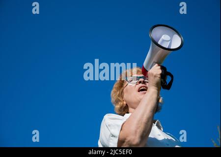 Emotional senior woman makes a speech in a megaphone on the outside. A ...