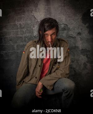 Junkie man with black hair and bottle with joint near old stone wall ...