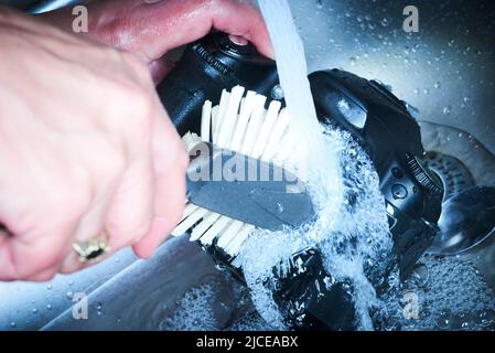 Female hands washing dslr camera as dirty dishes running water in the ...