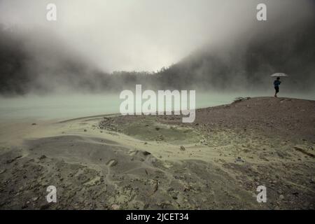 A visitor carrying an umbrella as he is walking on sandy landscape in a ...