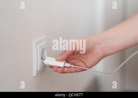 A young girl inserts a plug into an outlet. Young woman plugs the phone ...