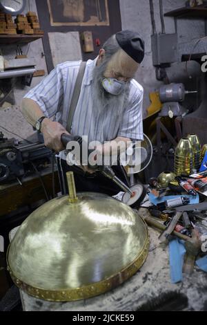 A Jewish silversmith and master craftsman works polishing the base of a ...