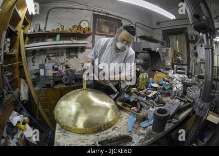 A Jewish silversmith and master craftsman works polishing the base of a ...