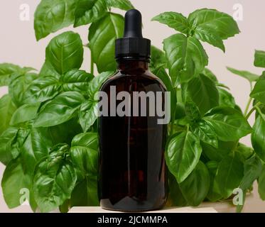 Brown glass bottle with a pipette against the background of green basil ...