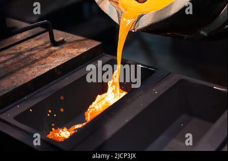 Molten silver is poured from the ladle into a black rectangular ...