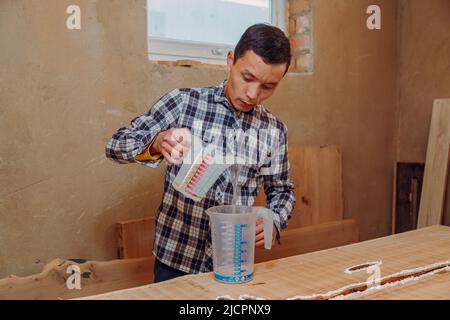 Carpenter pouring epoxy resin into liquid cup in a workshop. Process of ...