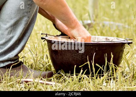 A man does his homework, cleans a cauldron in the backyard of a country ...