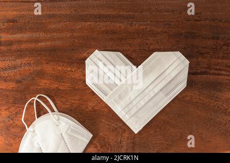 heart shape with white surgical masks on a rustic and natural wooden ...