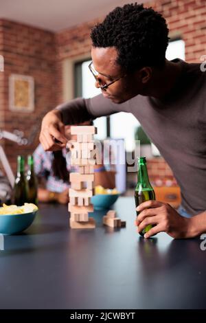 Focused young man carefully removing wood block from wooden tower ...