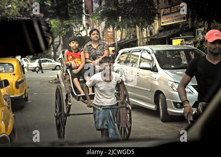 A rickshaw puller carrying a woman and a child passenger on a road in ...