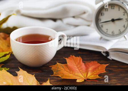 Alarm clock with knitted plaid and autumn leaves on wooden table ...