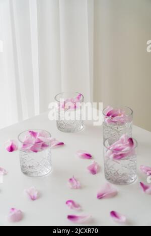 crystal glasses with tonic and floral petals on white surface and grey ...