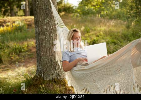Blonde woman using laptop at night at home making fish face with lips ...