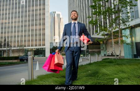 laughing man in formalwear with shopping bags and present box walk ...