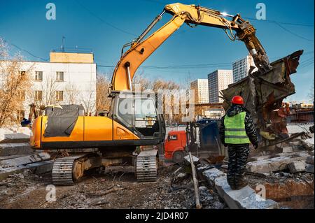 Excavator destroyer removes debris under worker control Stock Photo - Alamy