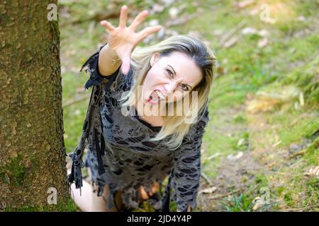 Snarling angry woman clawing at the camera in a forest reaching up with ...