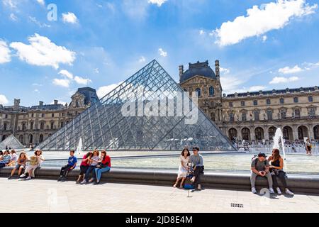 tired tourists rest sitting by the fountain next to the Louvre museum ...