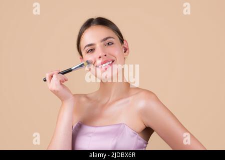 a beautiful young brunette is applying tonal powder with a makeup brush ...