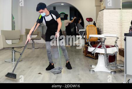 Young man hairdresser in mask cleaning floor in the beauty salon Stock ...
