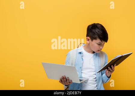 Asian schoolkid holding laptop and notebook isolated on yellow Stock ...