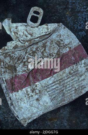 Squashed and split aluminium drinks can with rusty sides lying on ...