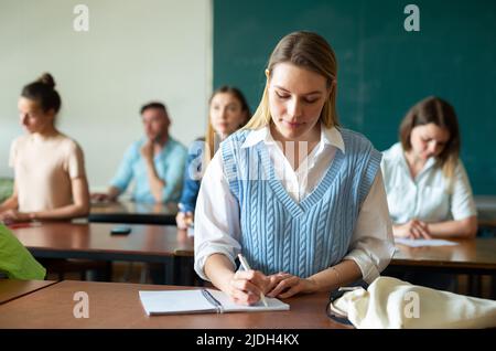 Portrait of female student writing lectures in workbooks in classroom ...