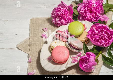 Macarons with a bouquet of peonies on white wooden background. Sweet ...