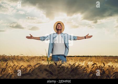 Happy farmer with arms outstretched standing in his growing wheat field ...
