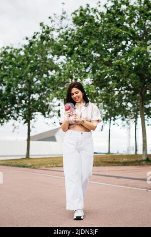 Young latin woman using smartphone holding umbrella at street Stock ...