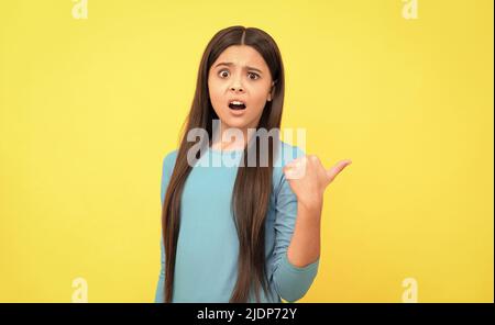 confused kid with long hair point finger on copy space on yellow ...