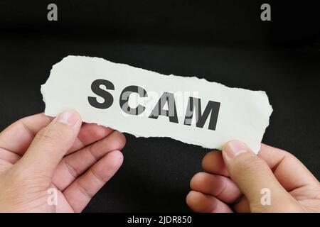 Scammed victim concept. Hand holding a piece of paper with word scam in ...