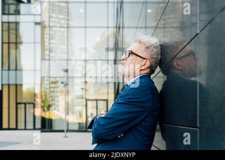 Thoughtful businessman leaning by wall outside building exterior Stock ...